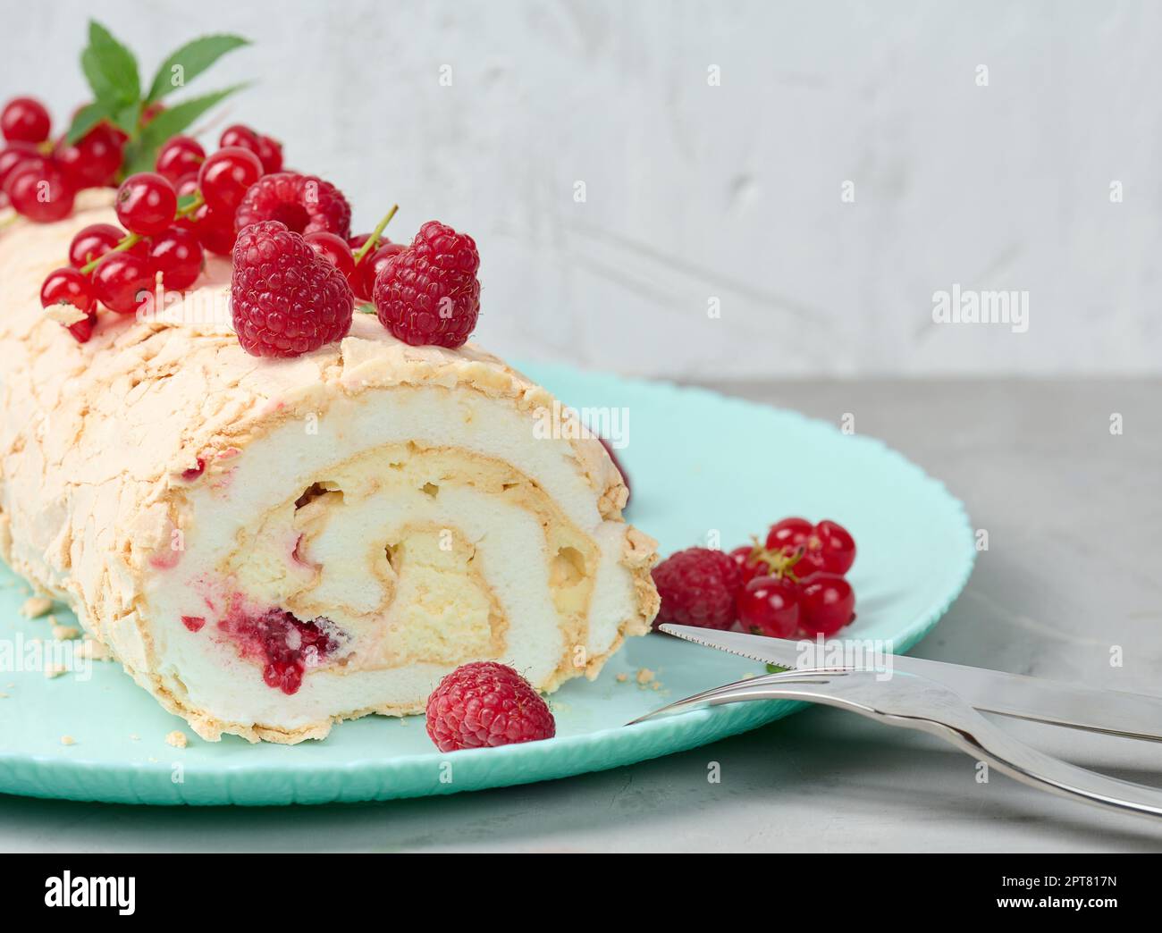 Baked meringue roll with red berries on a round plate, white background ...