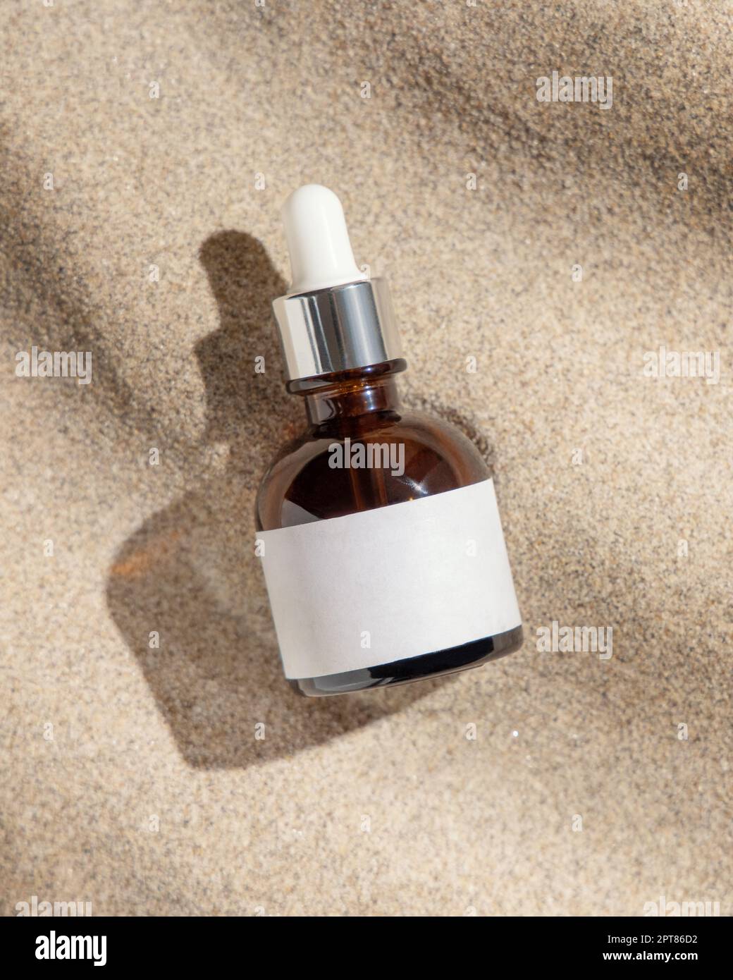 Dropper bottle with blank label on beige sand top view, hard light ...