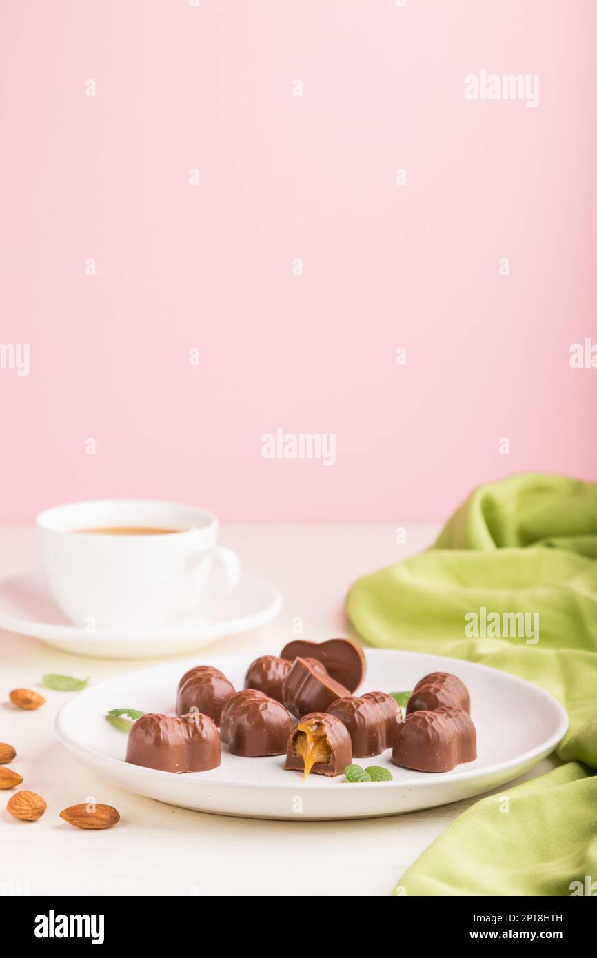 Chocolate caramel candies with almonds and a cup of coffee on a white ...