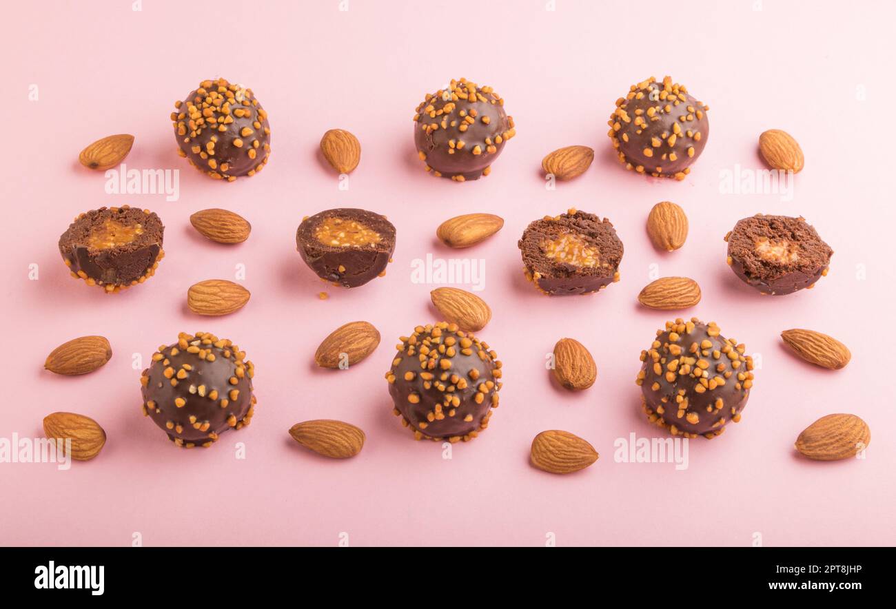 Chocolate caramel ball candies with almonds in a row on a pastel pink ...