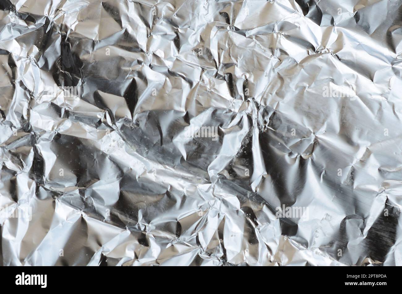 Thin wrinkled sheet of crushed tin aluminum silver foil background with ...
