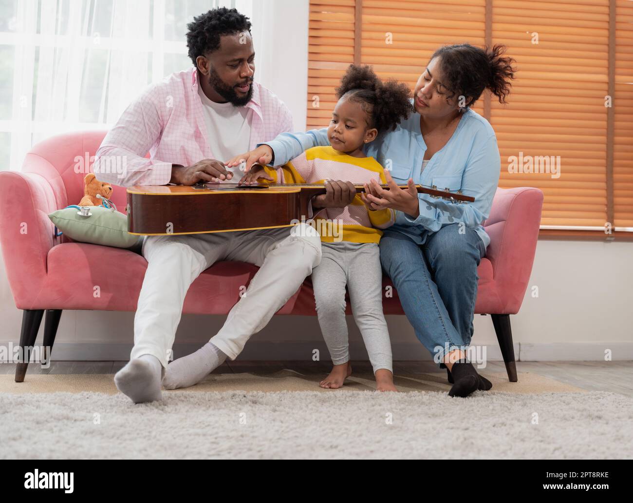Happy african family with little curly girl sitting relax on pink couch and playing guitar ...