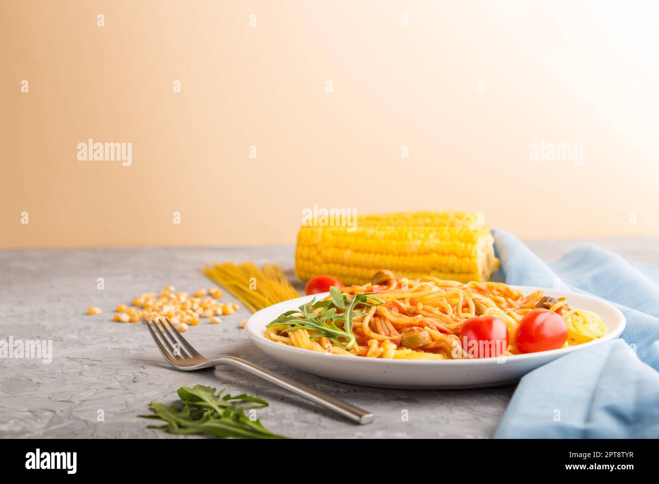 Corn noodles with tomato sauce and arugula on a gray and orange ...