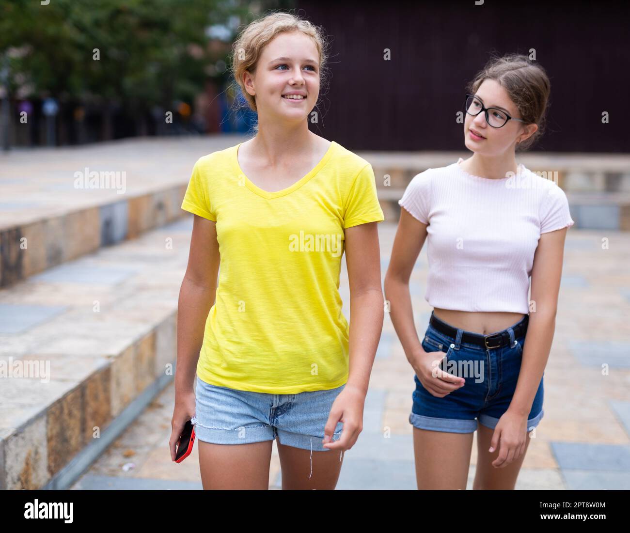 Portrait of two positive girls walking along street of summer city ...