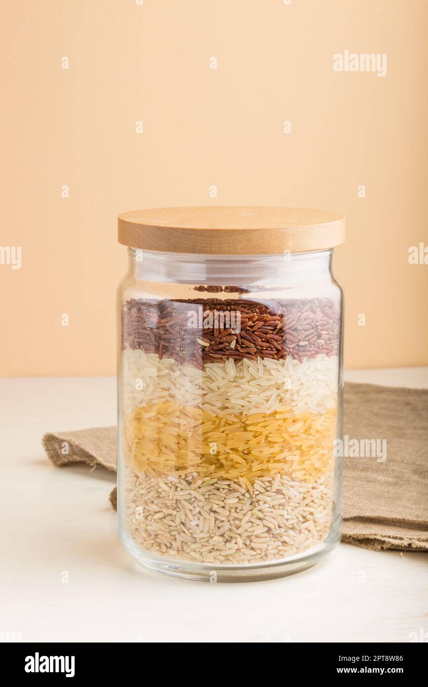 glass jar with different kinds of rice poured in layers on white and ...