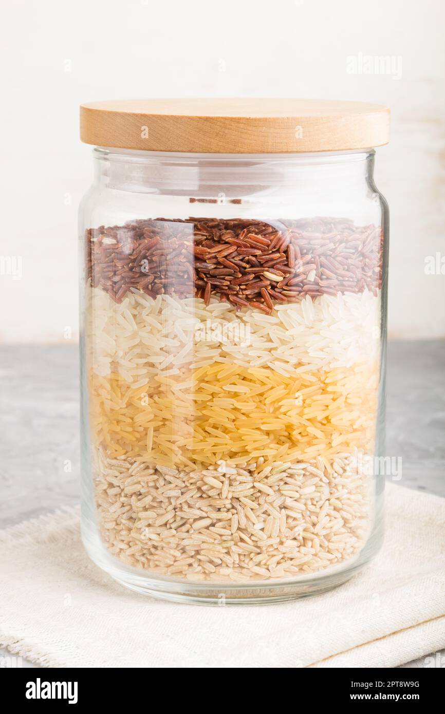 glass jar with different kinds of rice poured in layers on a gray and ...
