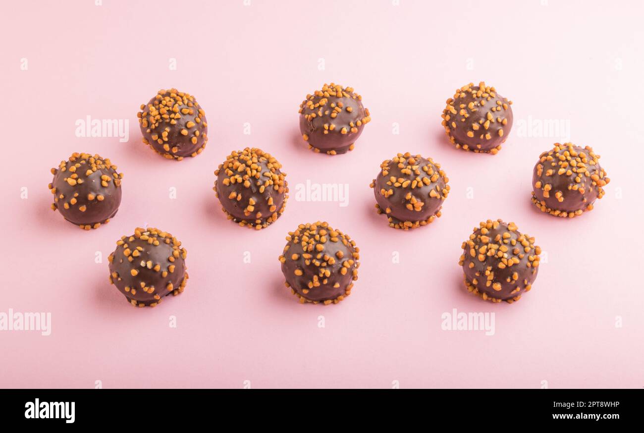 Chocolate caramel ball candies with almonds in a row on a pastel pink ...