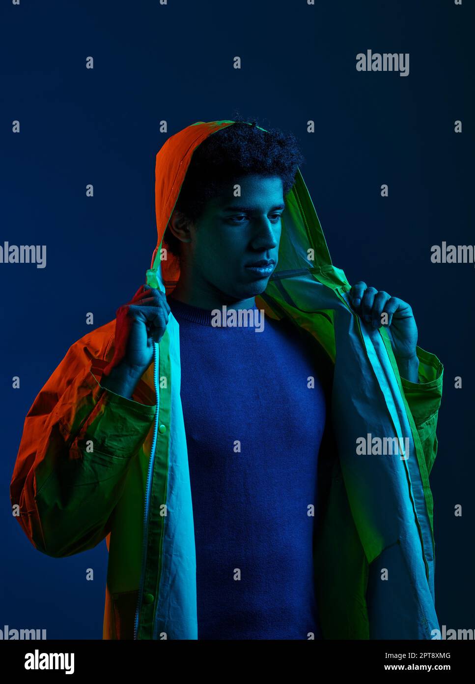 Young man put on waterproof raincoat outerwear over dark studio ...