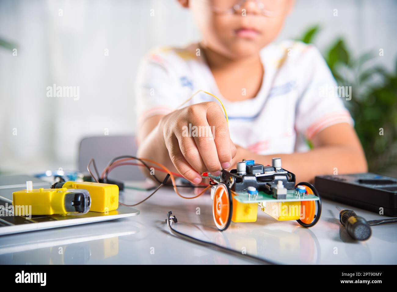 Asian kid boy plugging energy and signal cable to sensor chip with Arduino robot car, Little ...
