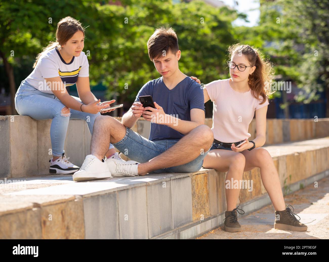 Teenage boy absorbed in phone, ignoring girls talking to him Stock ...