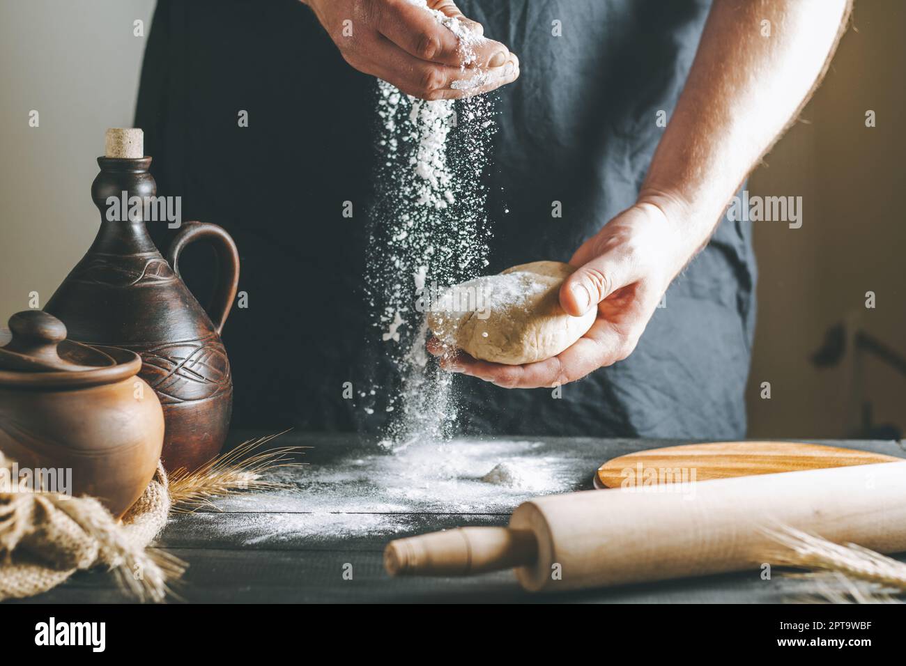 Male hands pour flour on the dough next to clay pot and oil bottle and ...