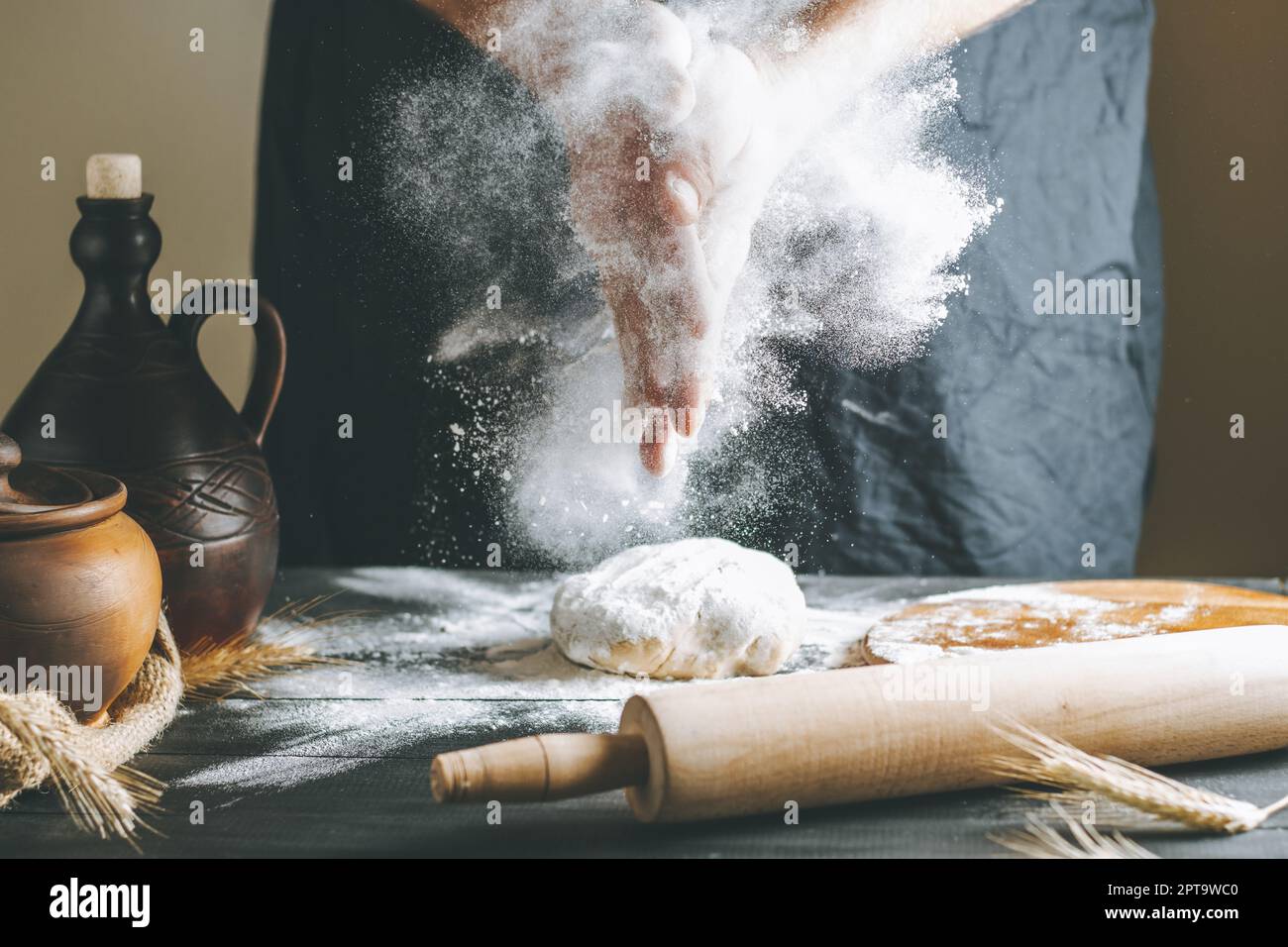 Male hands with flour clap over dough next to clay pot and oil bottle ...
