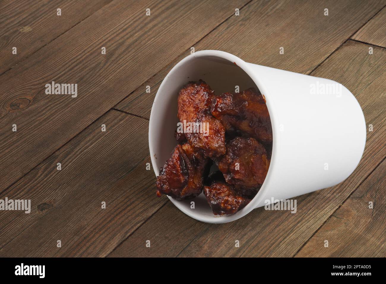 Cardboard container with fried chicken wings laying on wooden floor ...