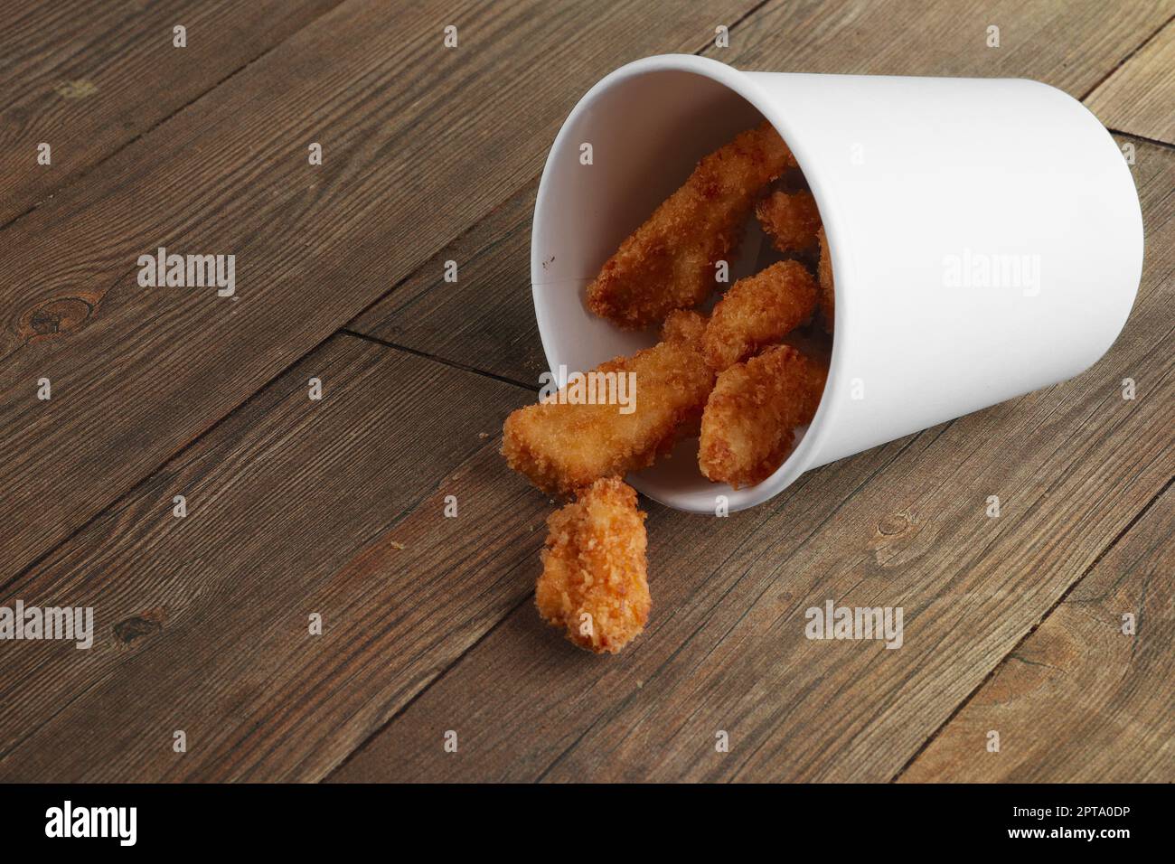 Cardboard container with fried chicken wings laying on wooden floor ...