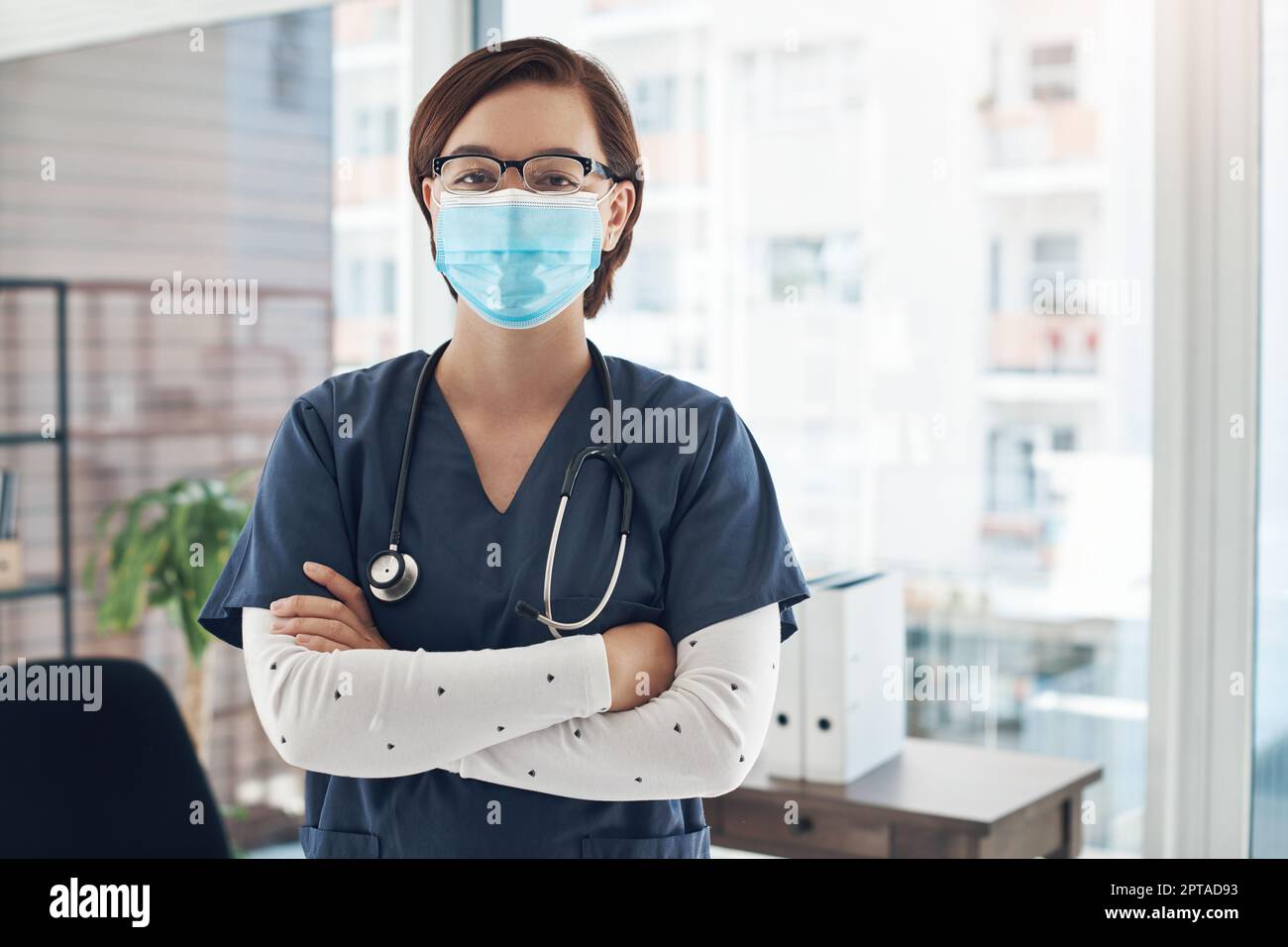 Protect yourself and others. a young doctor with her arms crossed while ...