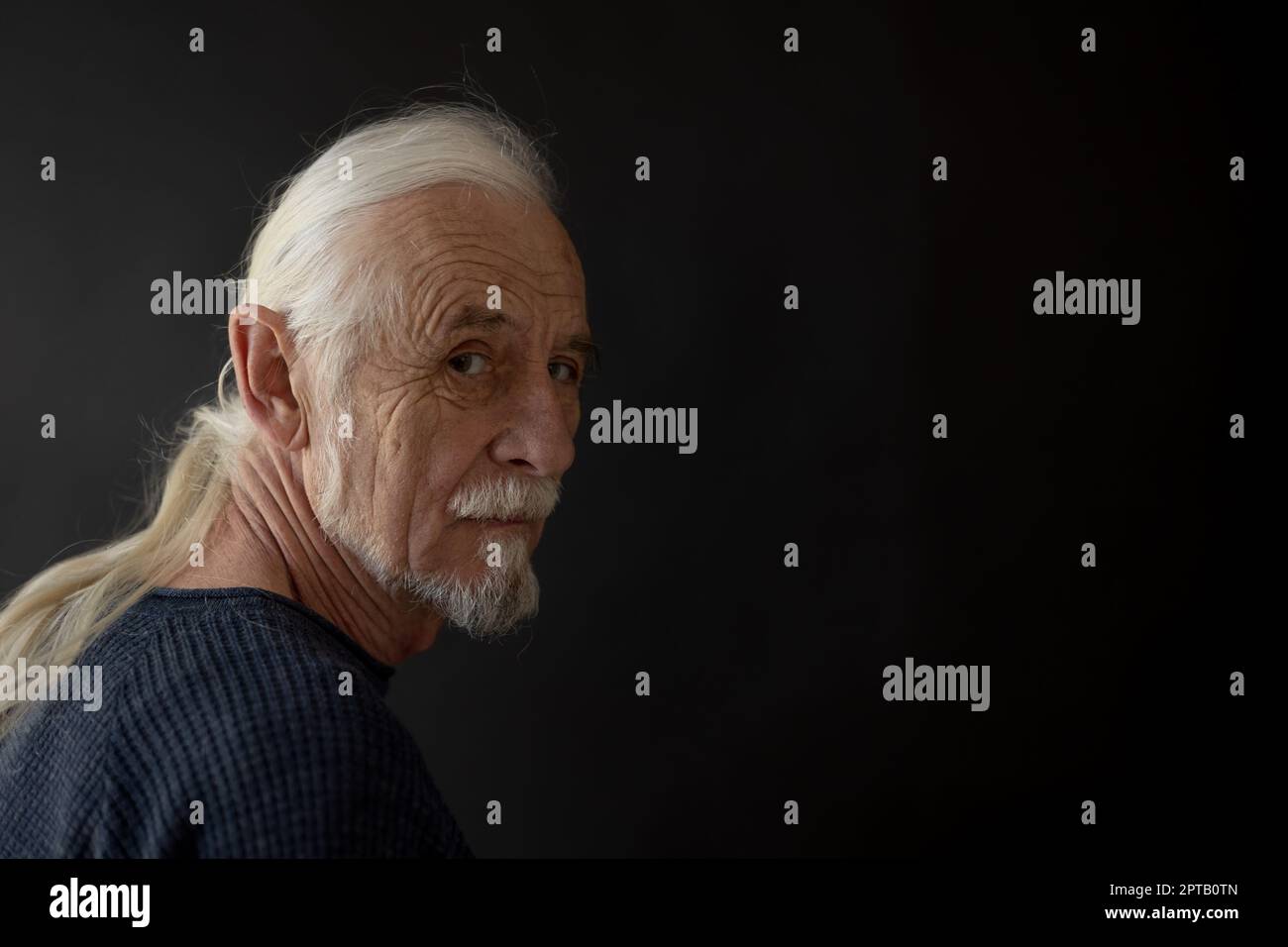 Low key studio portrait of beautiful old man with gray hair in a braid ...