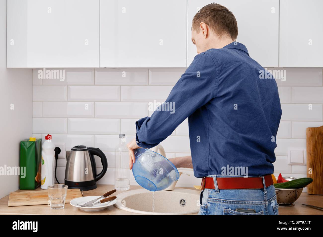 Back view of a middle aged man washes the dishes after cooking at home ...