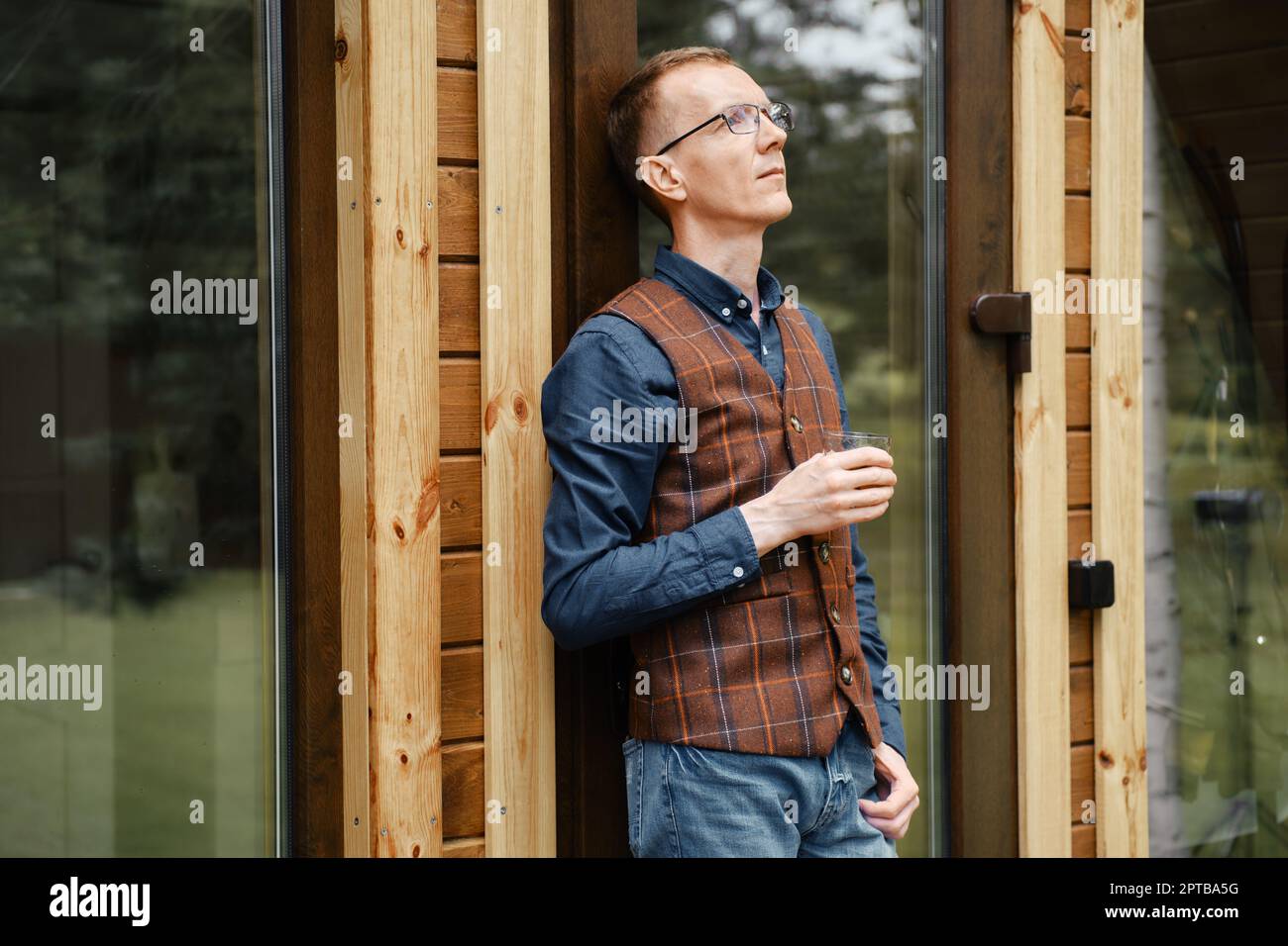 Pensive middle age man stands on the terrace of a cozy bungalow and ...
