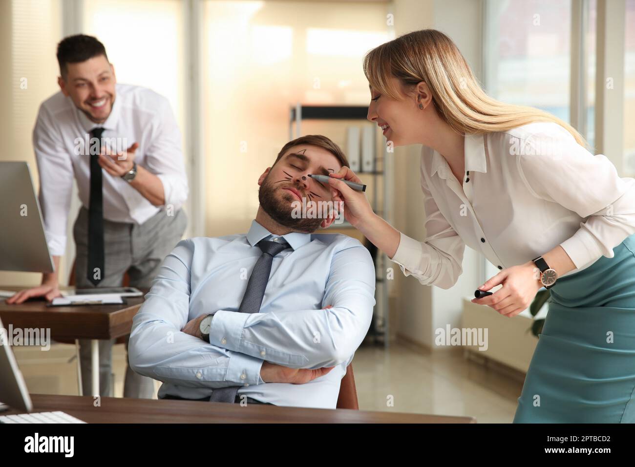 Young woman drawing on colleague's face while he sleeping in office ...