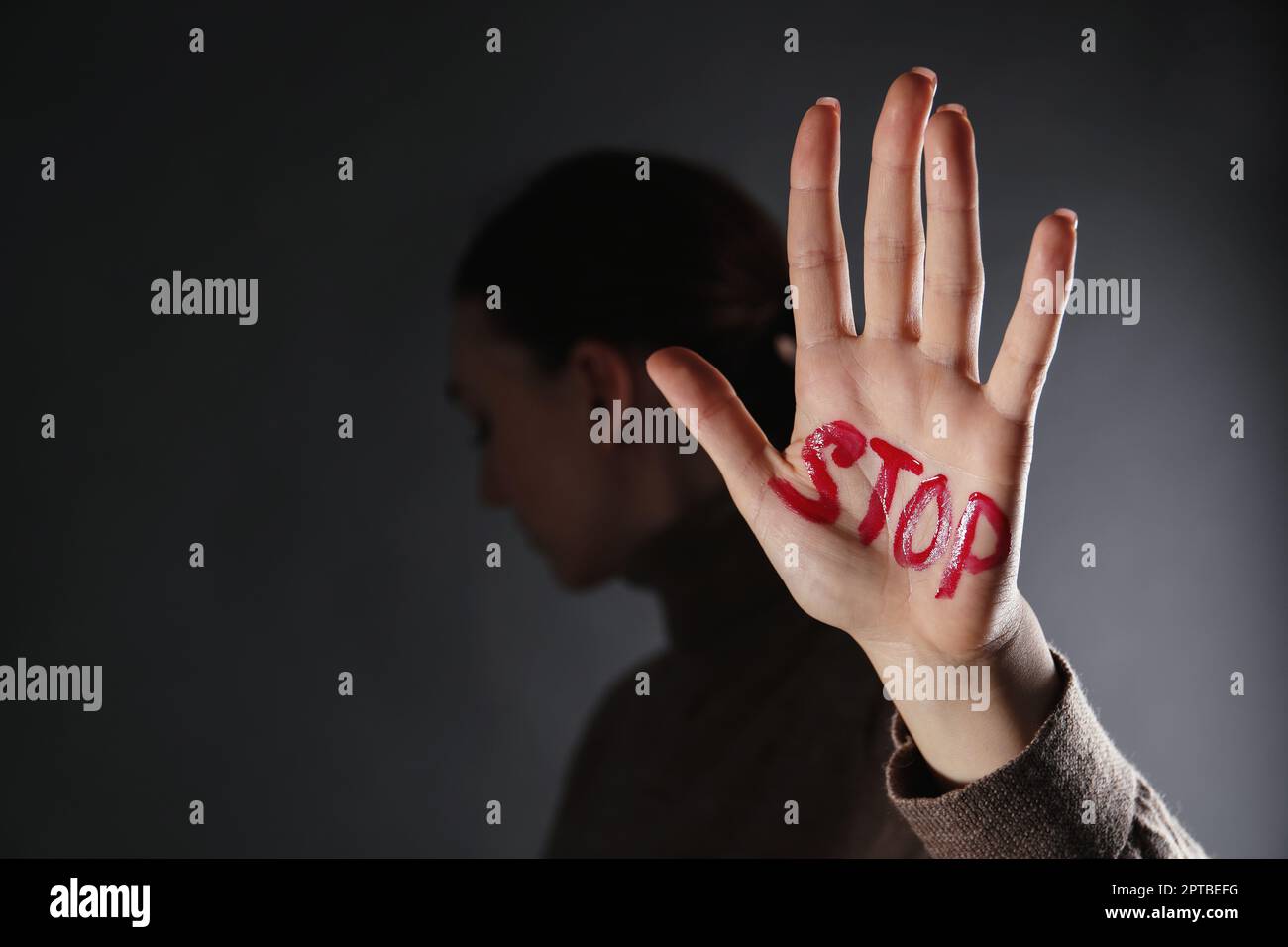 Woman with word Stop written on hand against black background, closeup ...