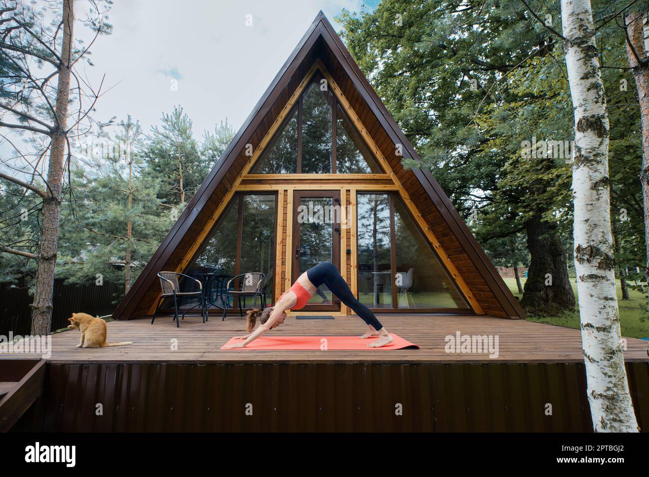 Flexible woman standing in dog's face-down pose on wooden terrace of ...