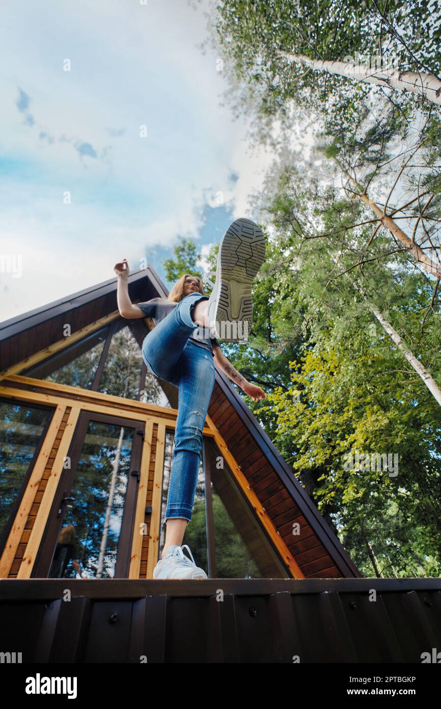 Joyful woman jumps off the porch of a-frame cabin, low angle view Stock ...
