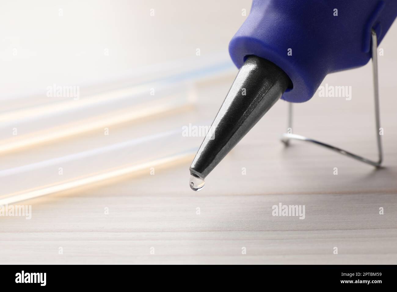 Melted glue dripping from hot gun on white table, closeup. Space for ...