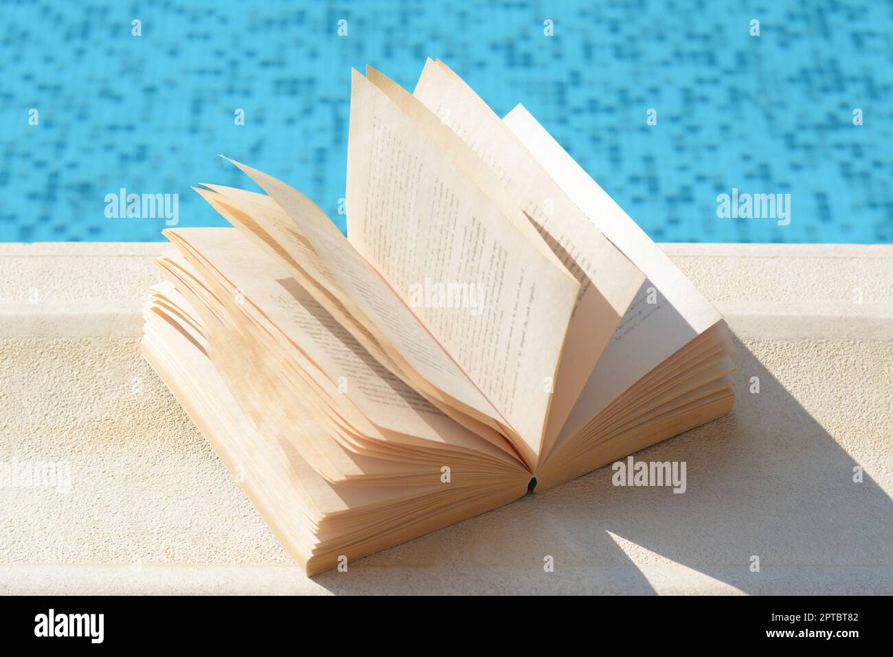 Open book on swimming pool edge during sunny day Stock Photo - Alamy
