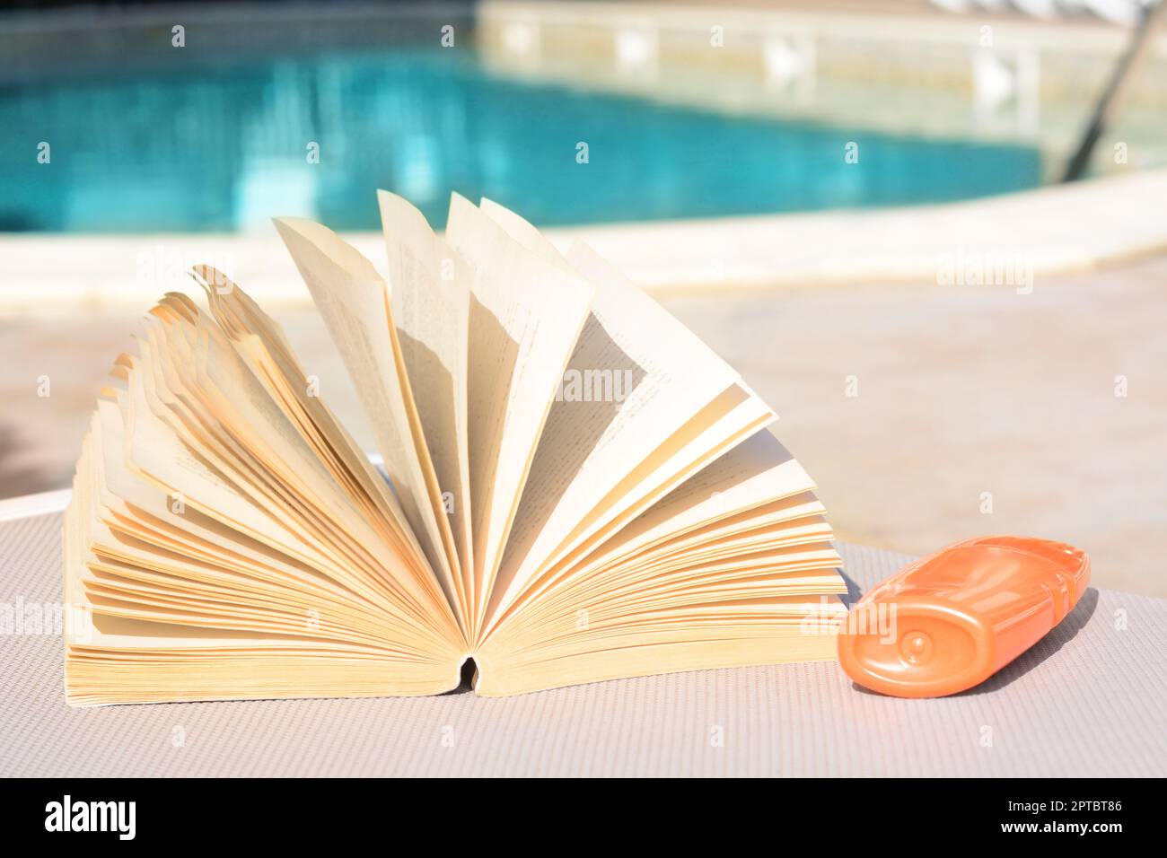 Open book on deck chair near swimming pool Stock Photo - Alamy