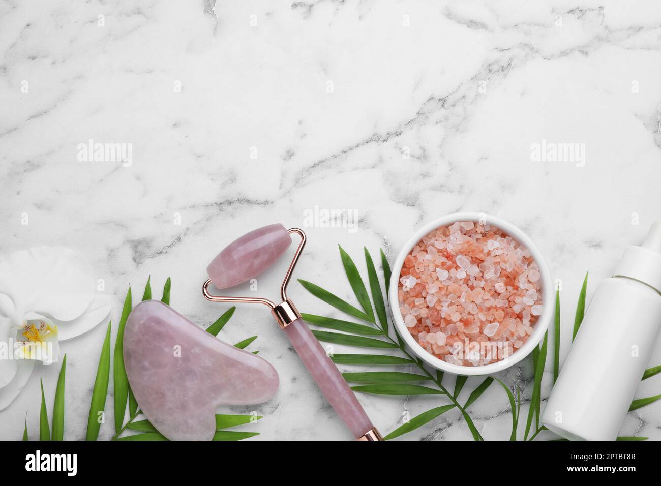 Flat lay composition with gua sha stone and face roller on white marble ...