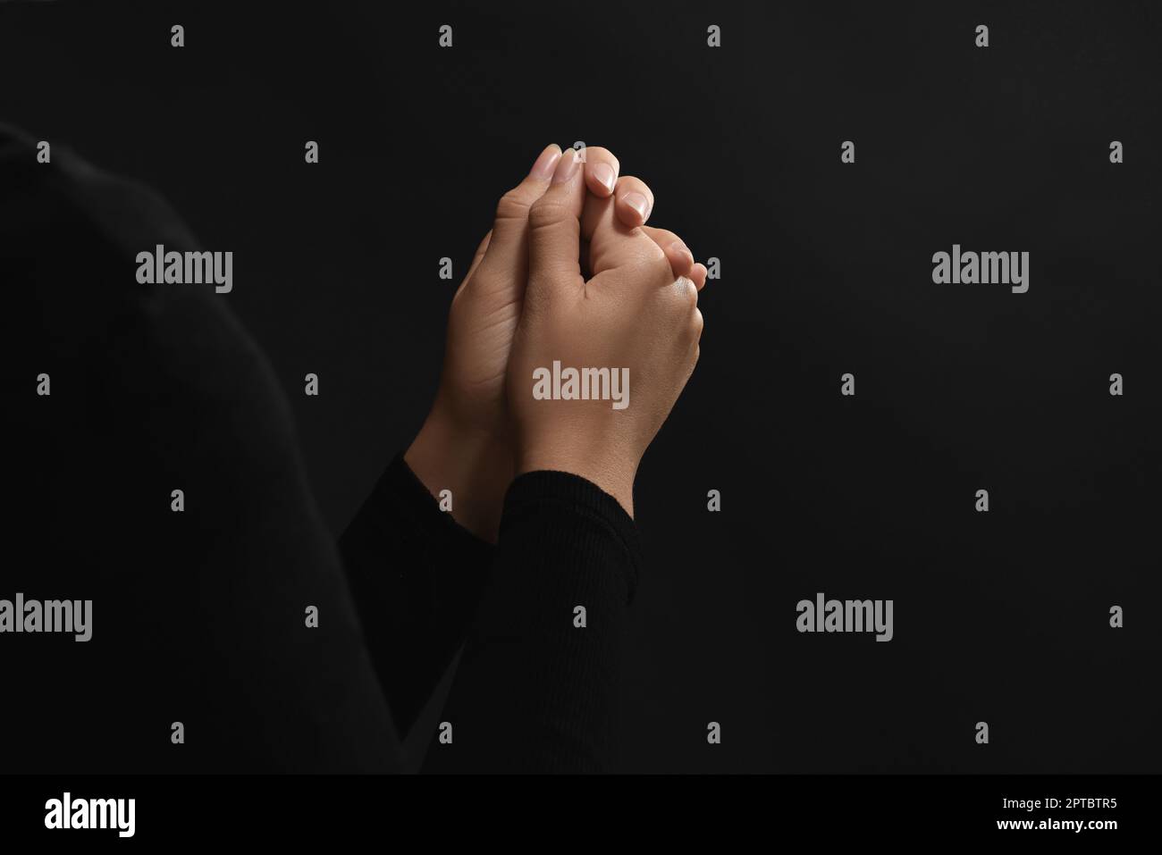 Woman holding hands clasped while praying against black background ...