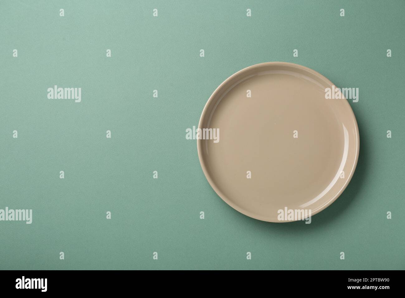 Clean beige plate on light green background, top view. Space for text ...