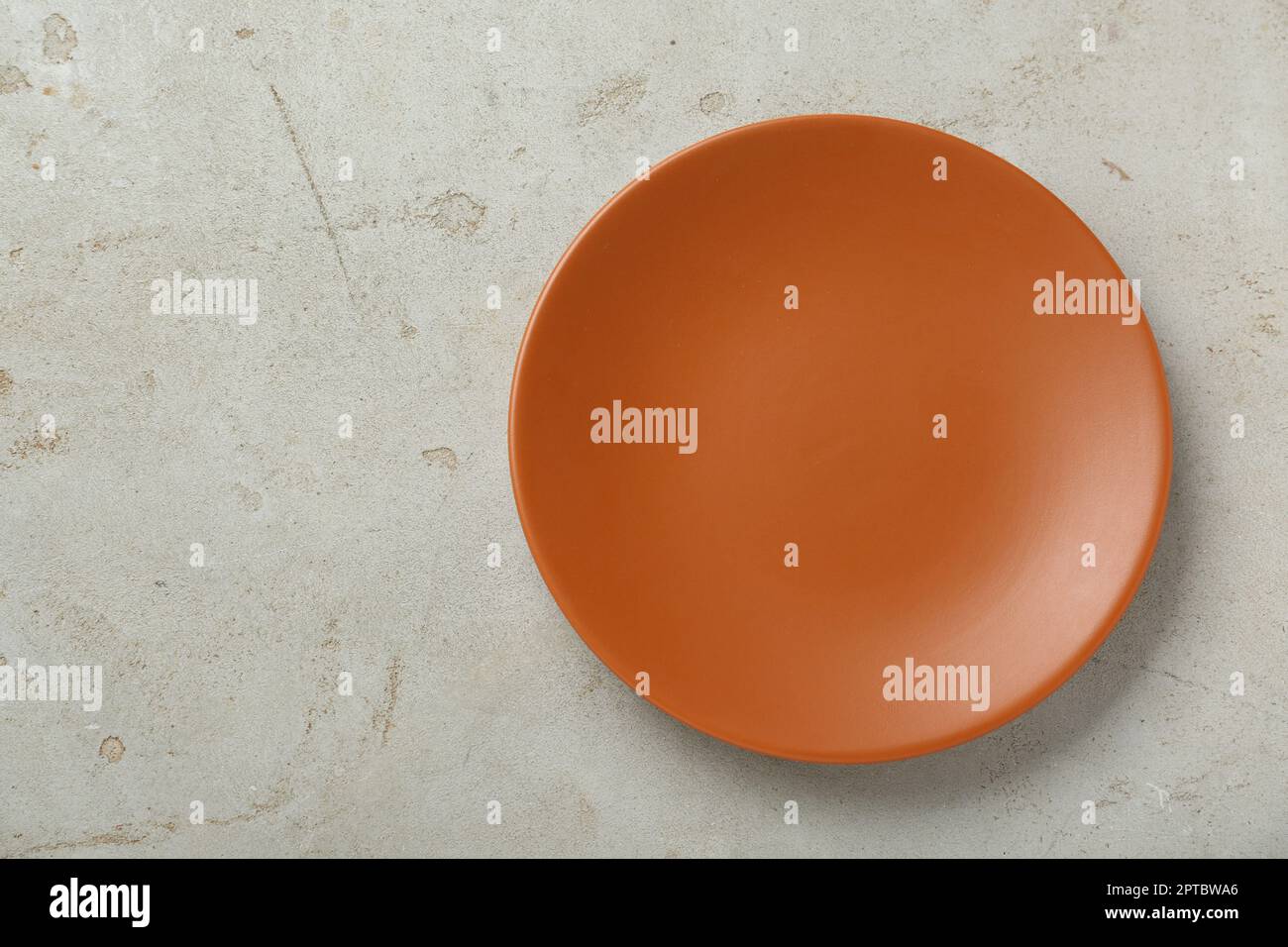 Empty orange ceramic plate on light grey table, top view. Space for ...