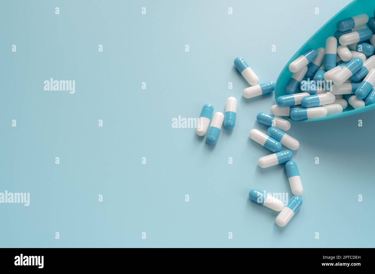 Blue and white capsules pill in plastic spoon and on blue background ...