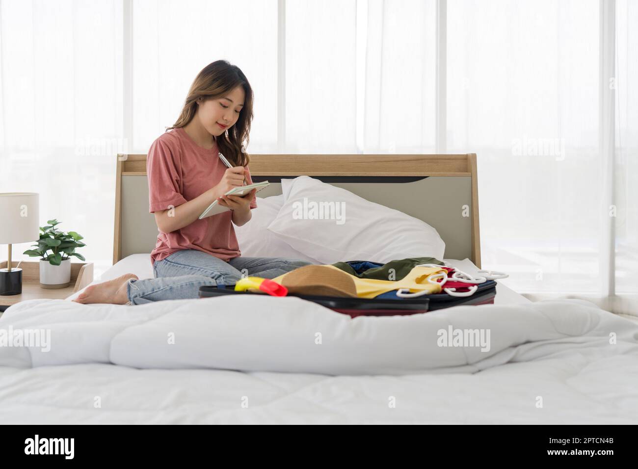 Asian teenage in casual clothes make a checklist while packing her ...