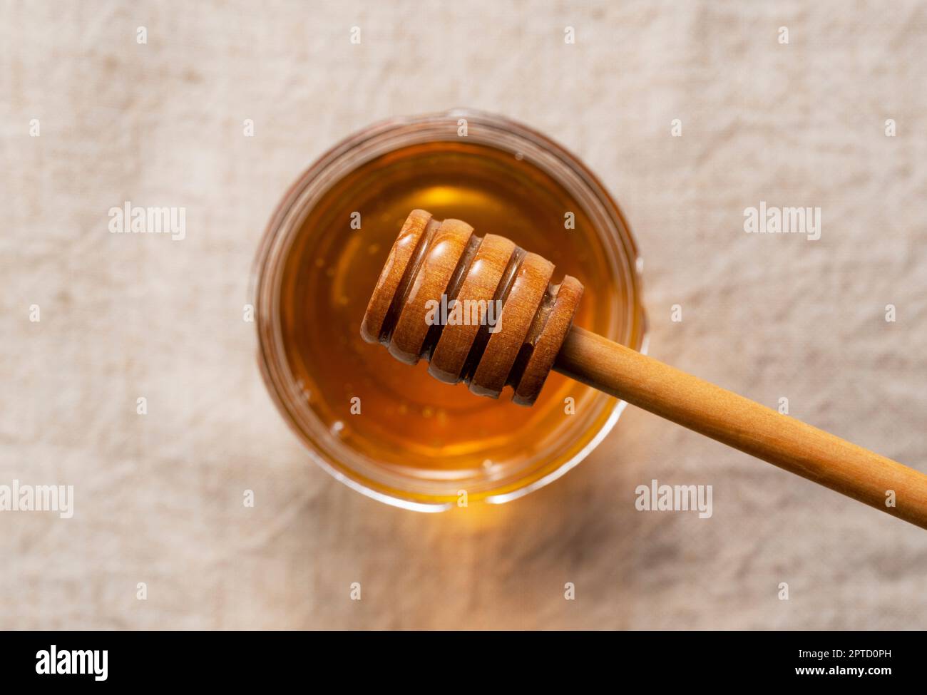 Honey in glass container and wooden honey dipper on cloth background ...