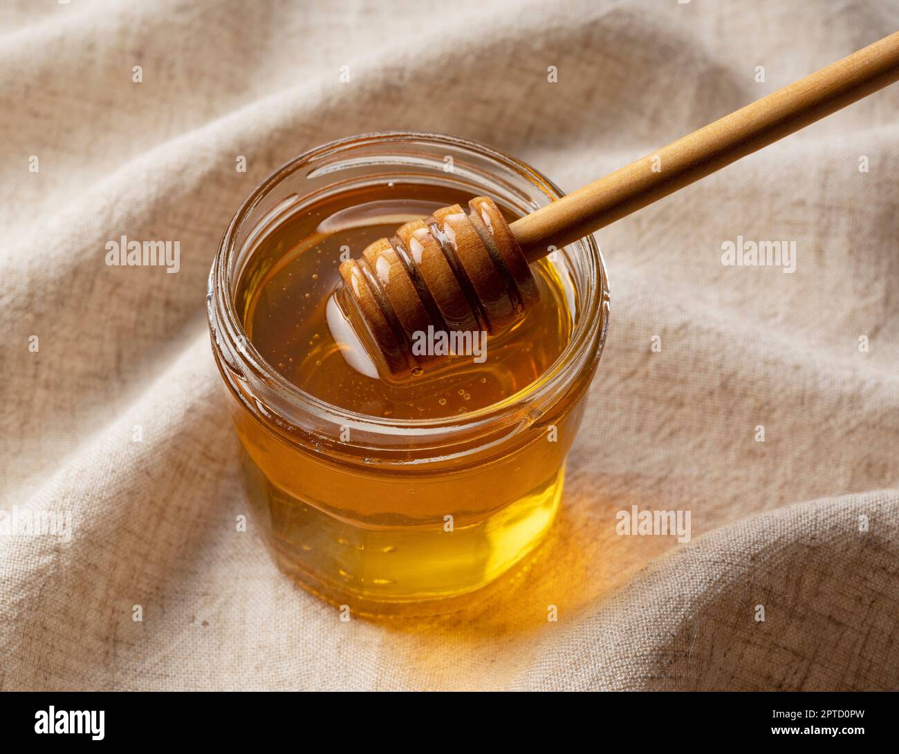 Honey in glass container and wooden honey dipper on cloth background ...