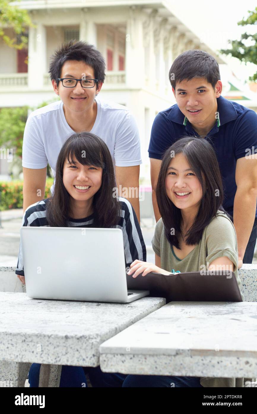 Our study group is outside today. Four young students sharing a laptop ...