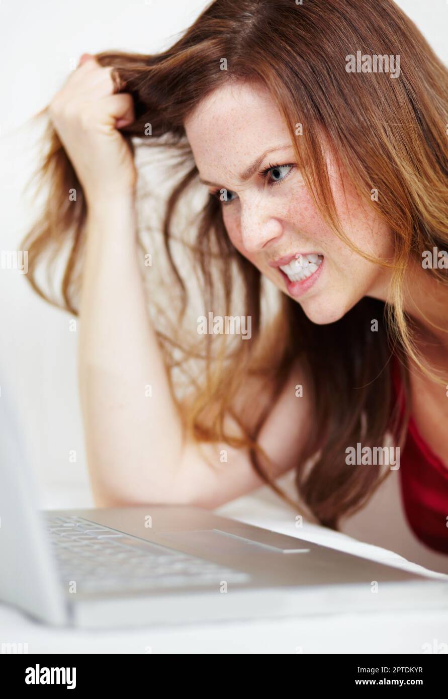 Internet frustration. A frustrated young woman pulling her hair out while working on a laptop ...