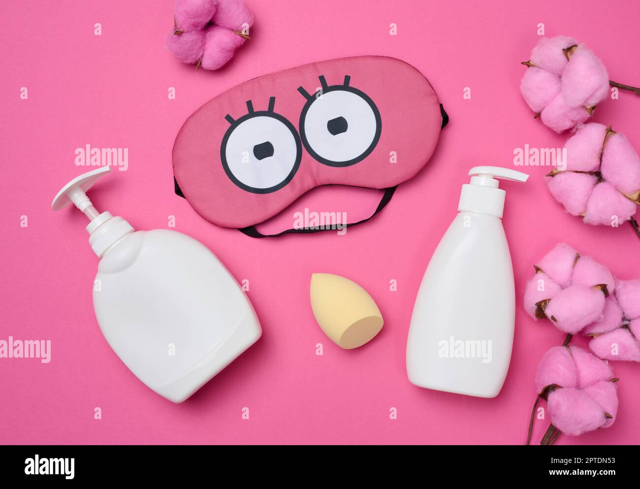 Textile sleep mask, sponge and plastic bottles with cosmetics on a pink ...