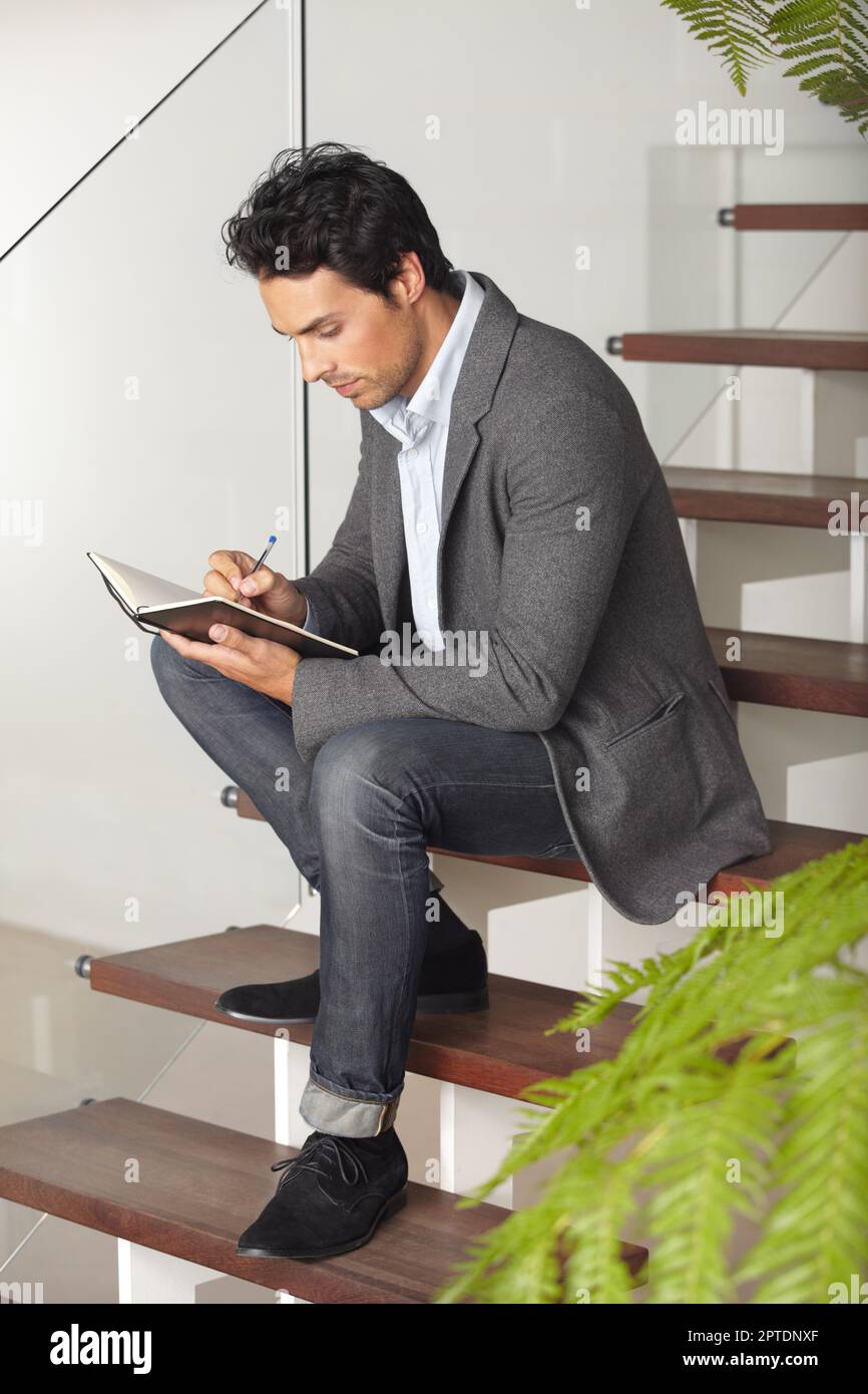 Making appointments. A young businessman sitting on a staircase writing ...