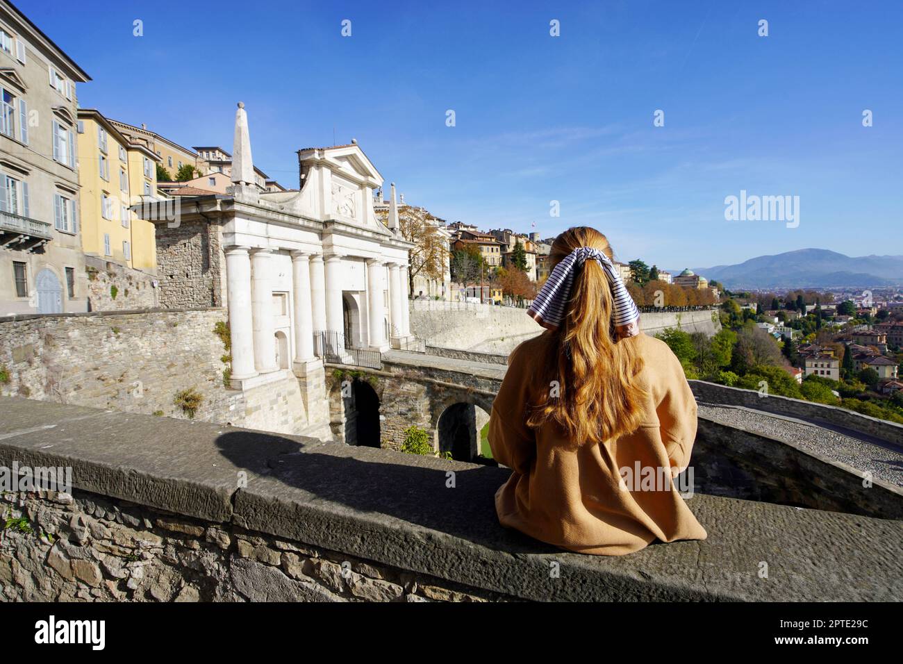 Tourism in Bergamo, Italy. Young woman sitting on Bergamo wall looking ...