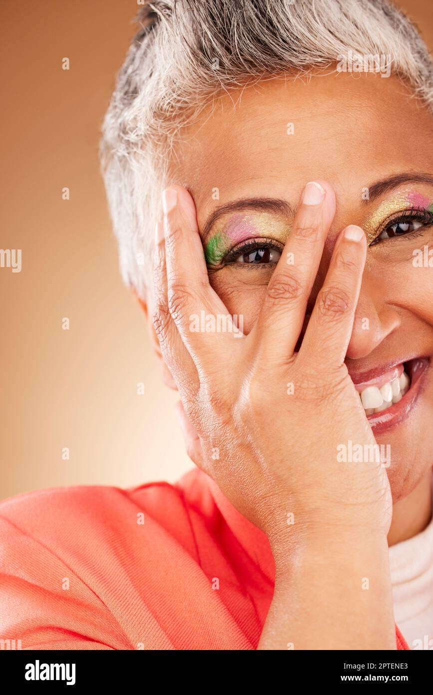 Makeup, comic and senior woman creative with color for face against a brown studio background ...