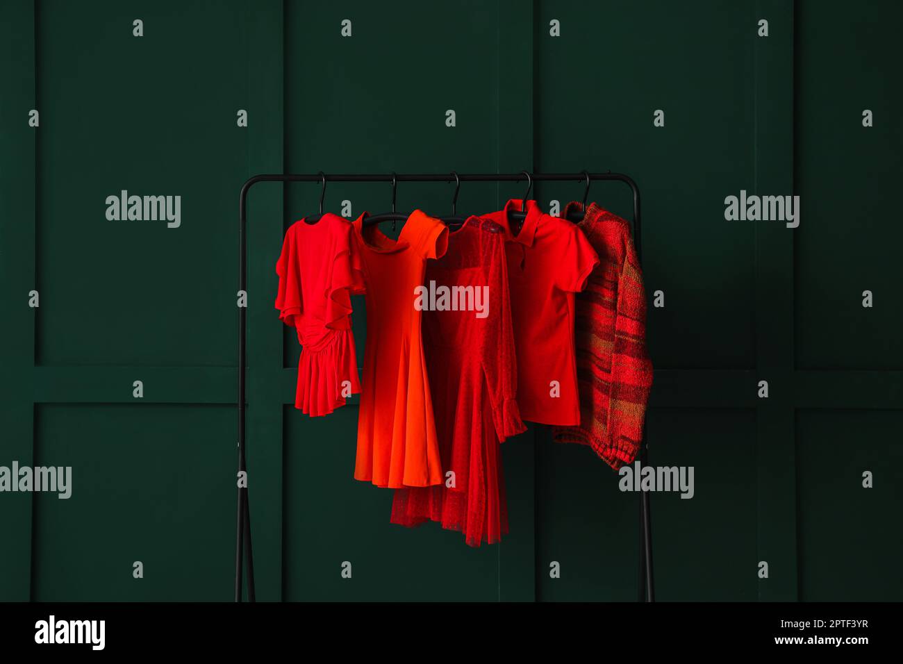 Rack with red female clothes near green wall Stock Photo - Alamy