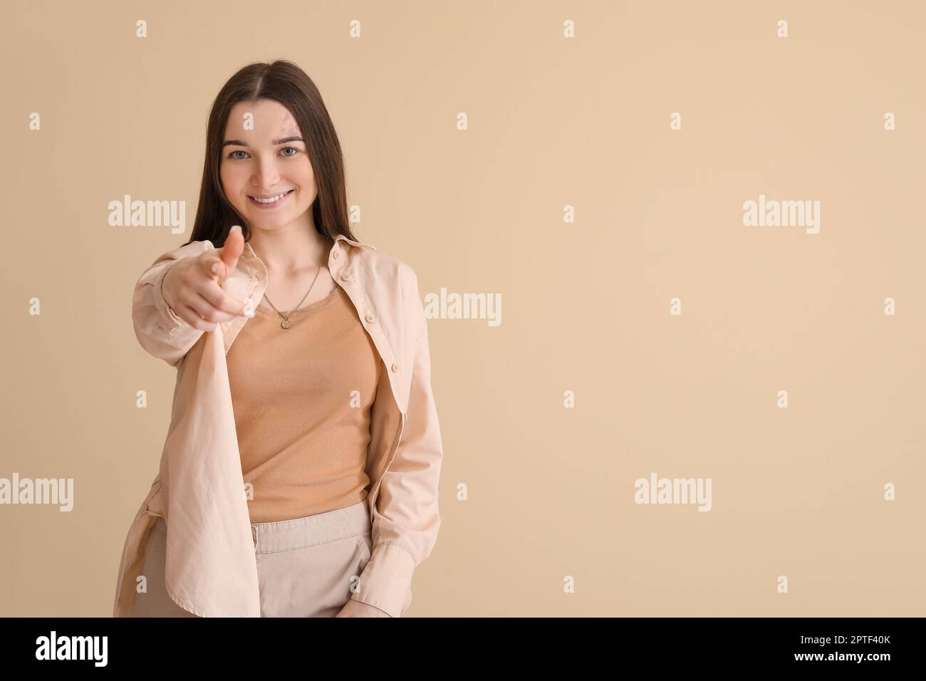 Young woman pointing at viewer on beige background Stock Photo - Alamy