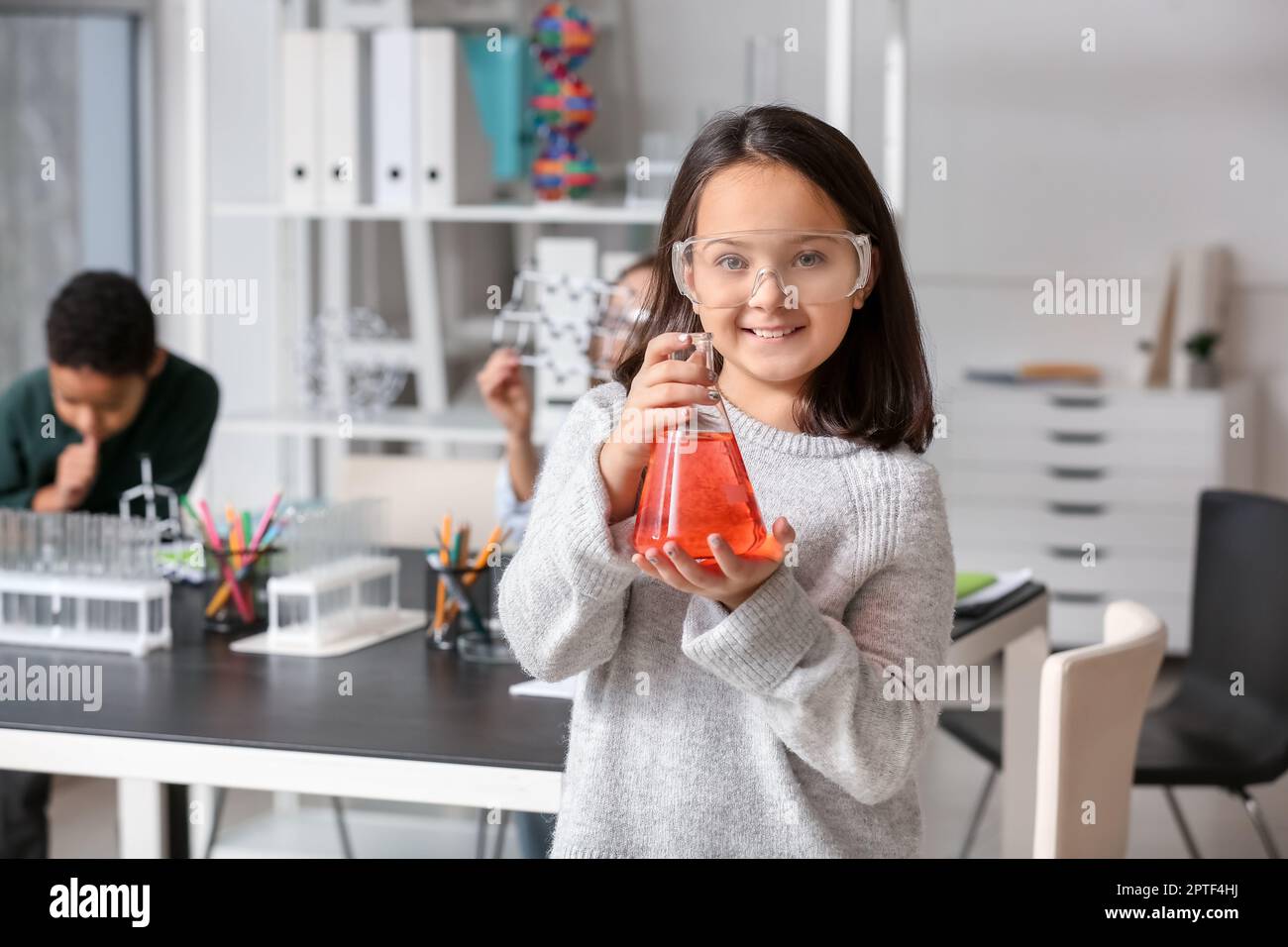Little girl with safety goggles and conical flask in science classroom ...