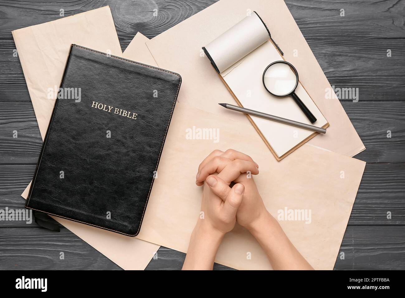 Praying woman with Holy Bible, notebook and paper sheets on dark wooden ...