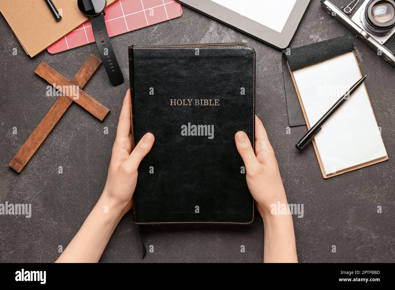 Woman with Holy Bible, cross, notebooks and devices on dark background ...