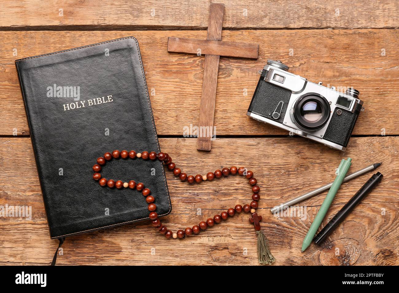 Holy Bible with photo camera, pens, prayer beads and cross on wooden ...