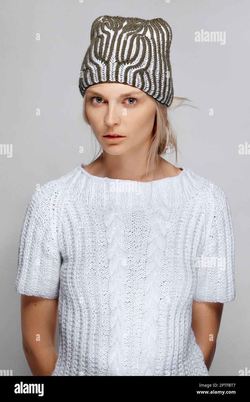 Pretty fashion model in white sweater and knitted hat hides hands ...